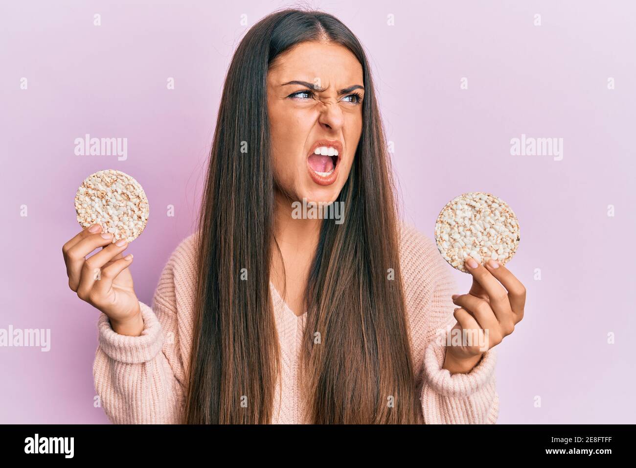 Beautiful hispanic woman eating healthy rice crackers angry and mad ...