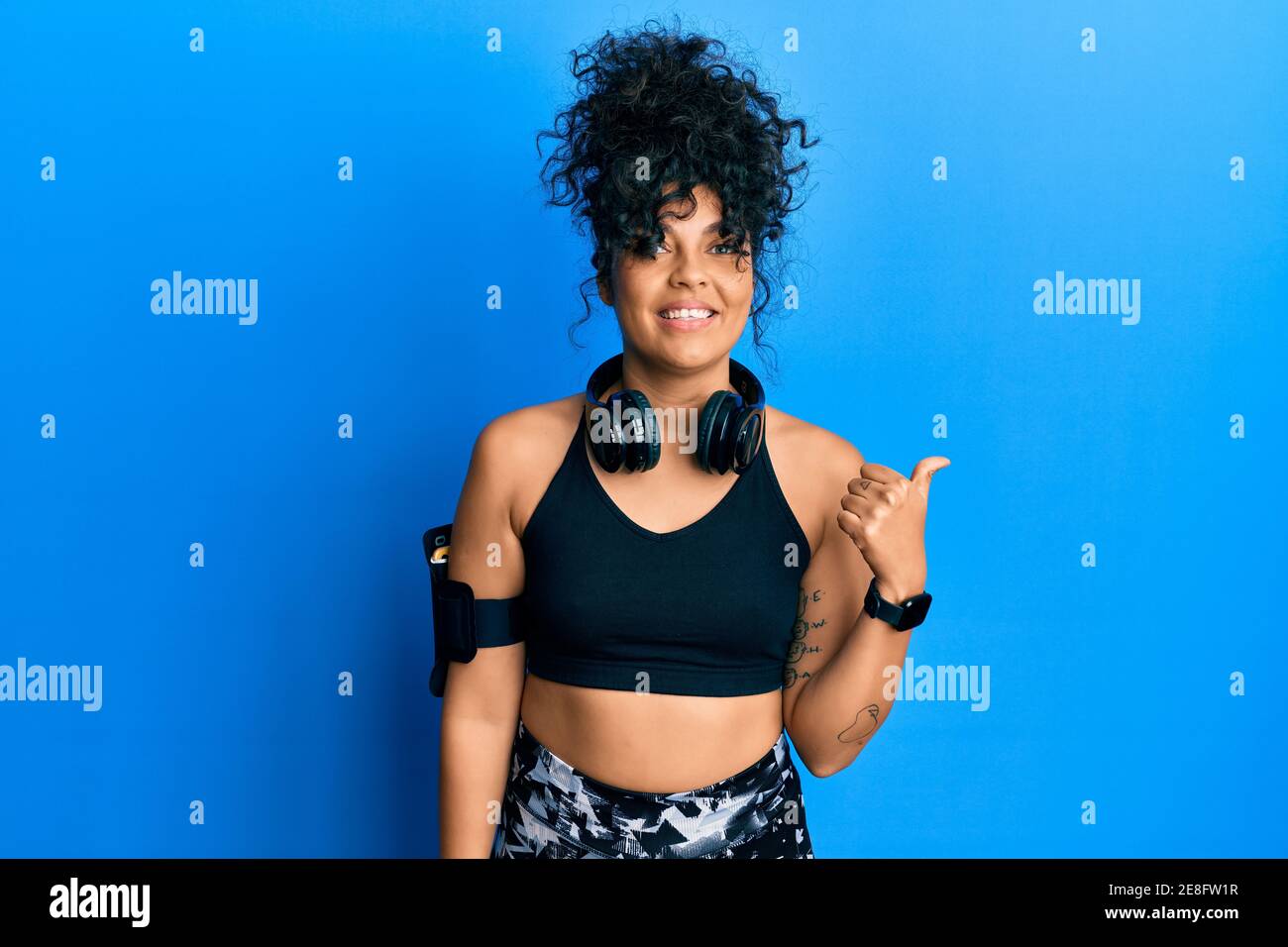 Young hispanic woman wearing gym clothes and using headphones smiling ...
