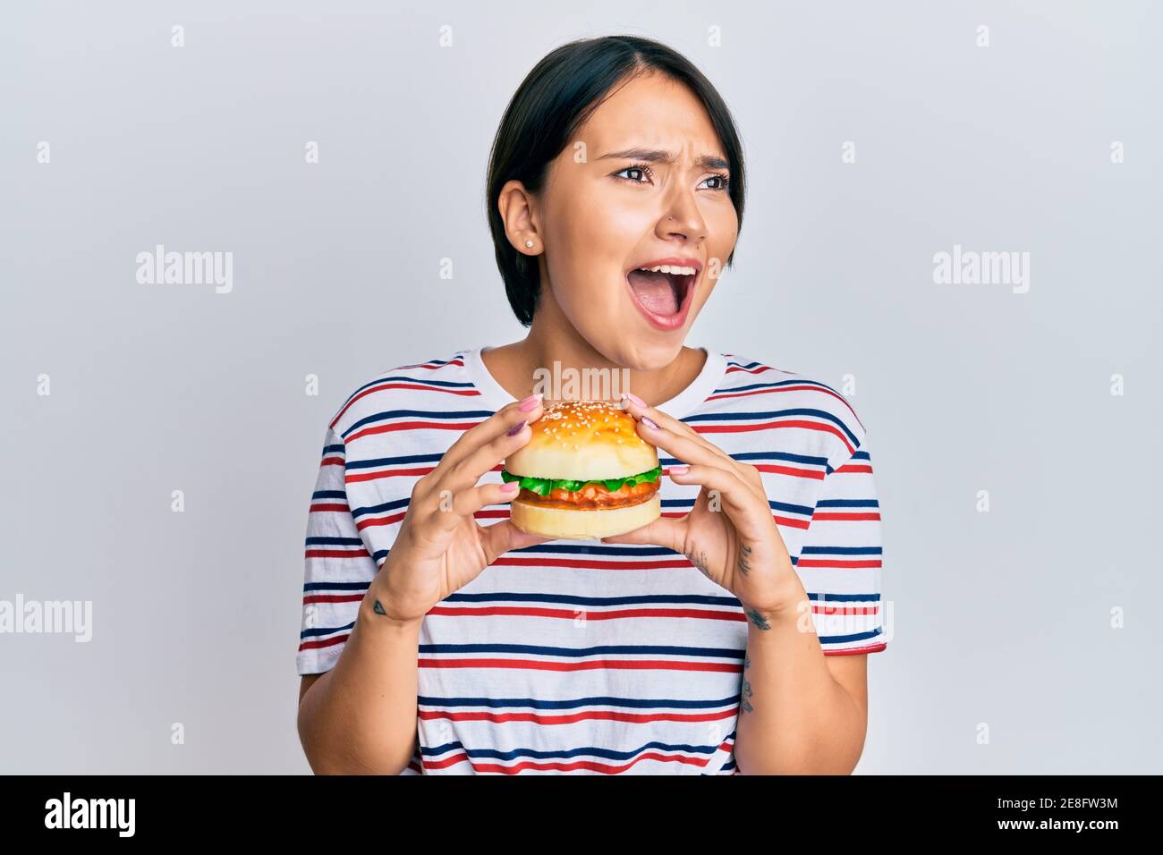 Beautiful young woman with short hair eating hamburger angry and mad ...