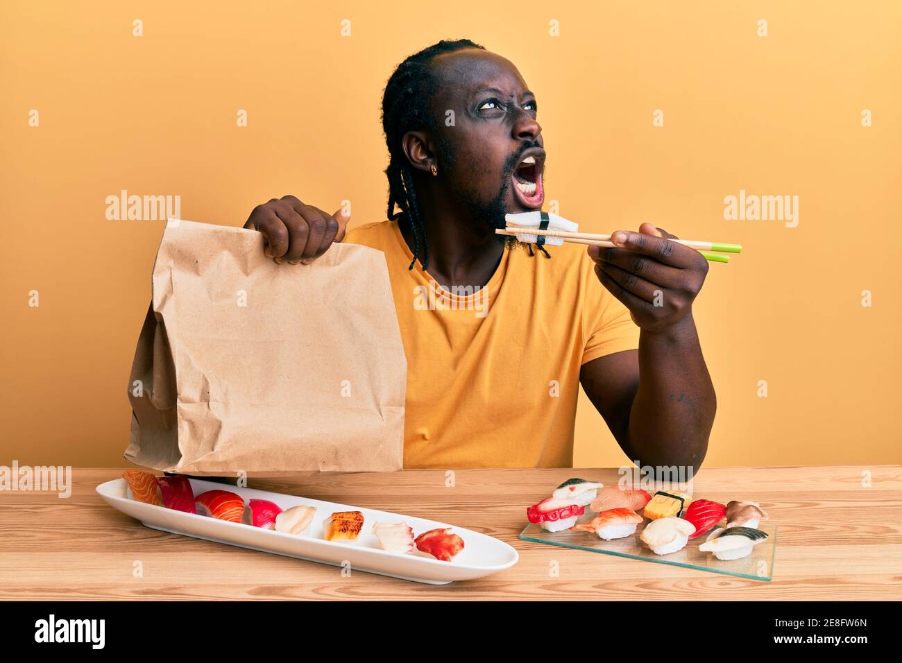 Handsome young black man eating take away sushi sitting on the table ...