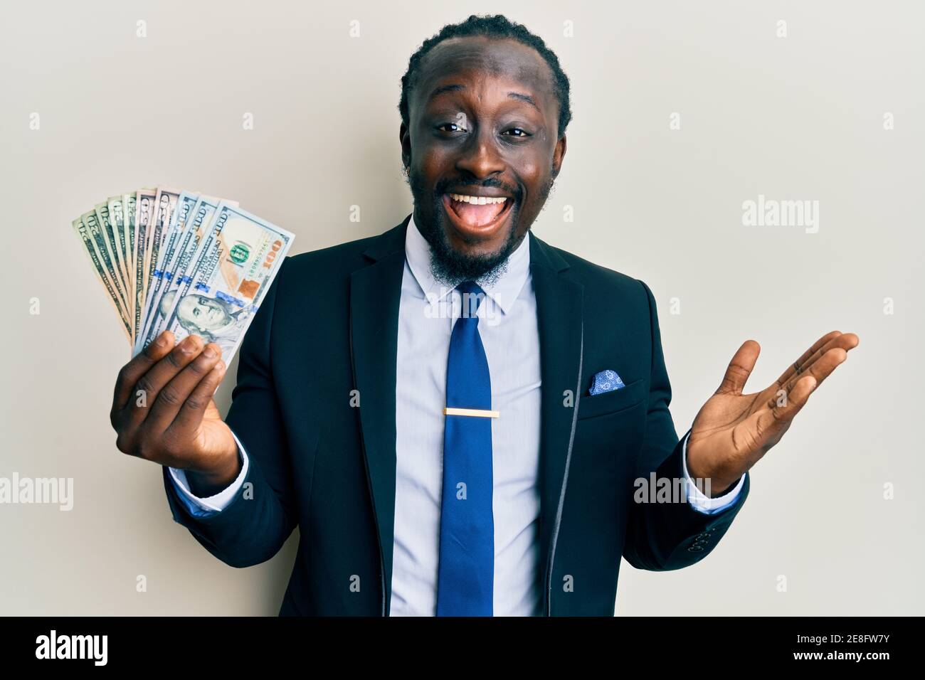 Handsome young black man wearing business suit and tie holding dollars ...