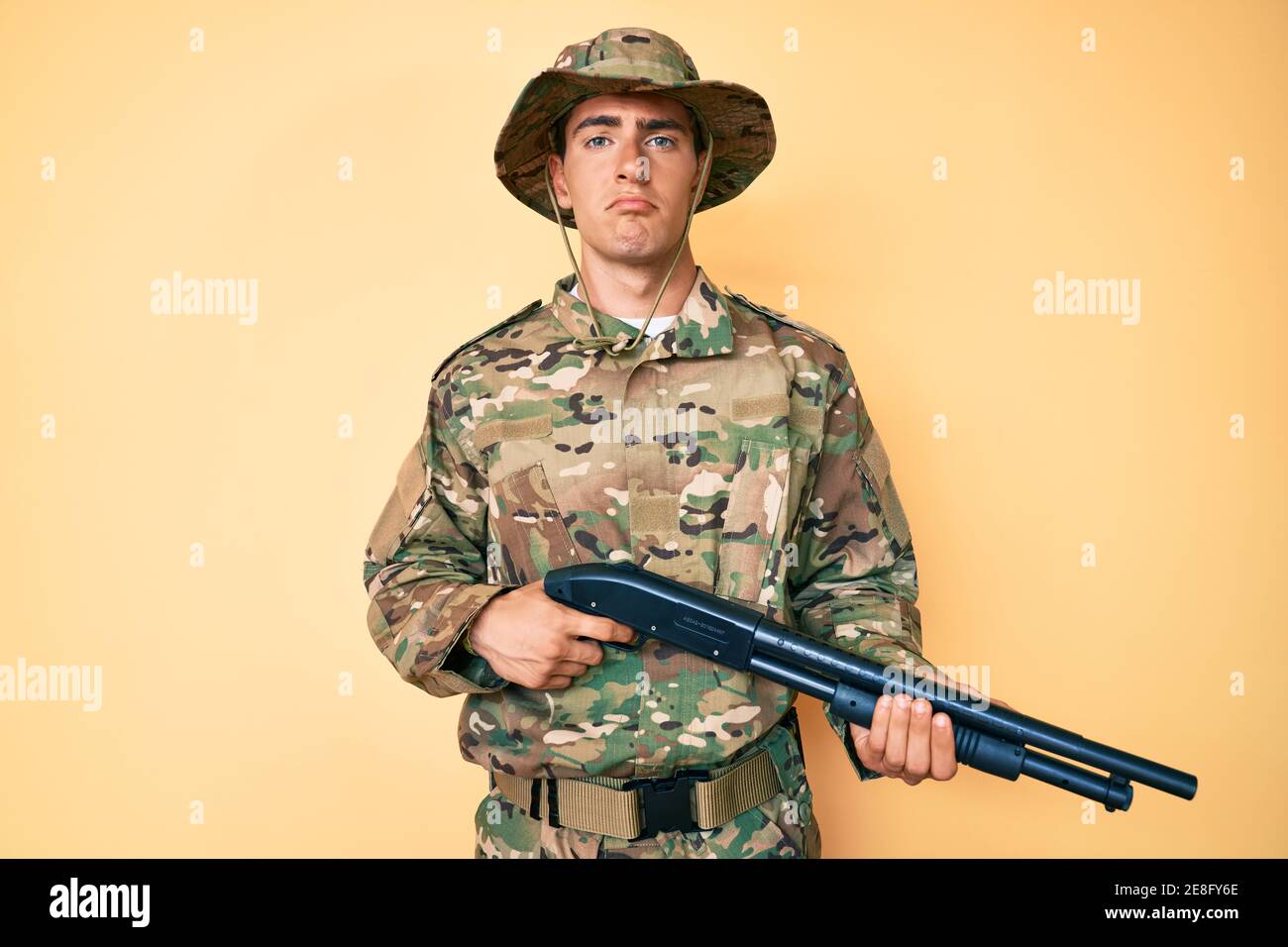 Young handsome man wearing camouflage army uniform holding shotgun ...