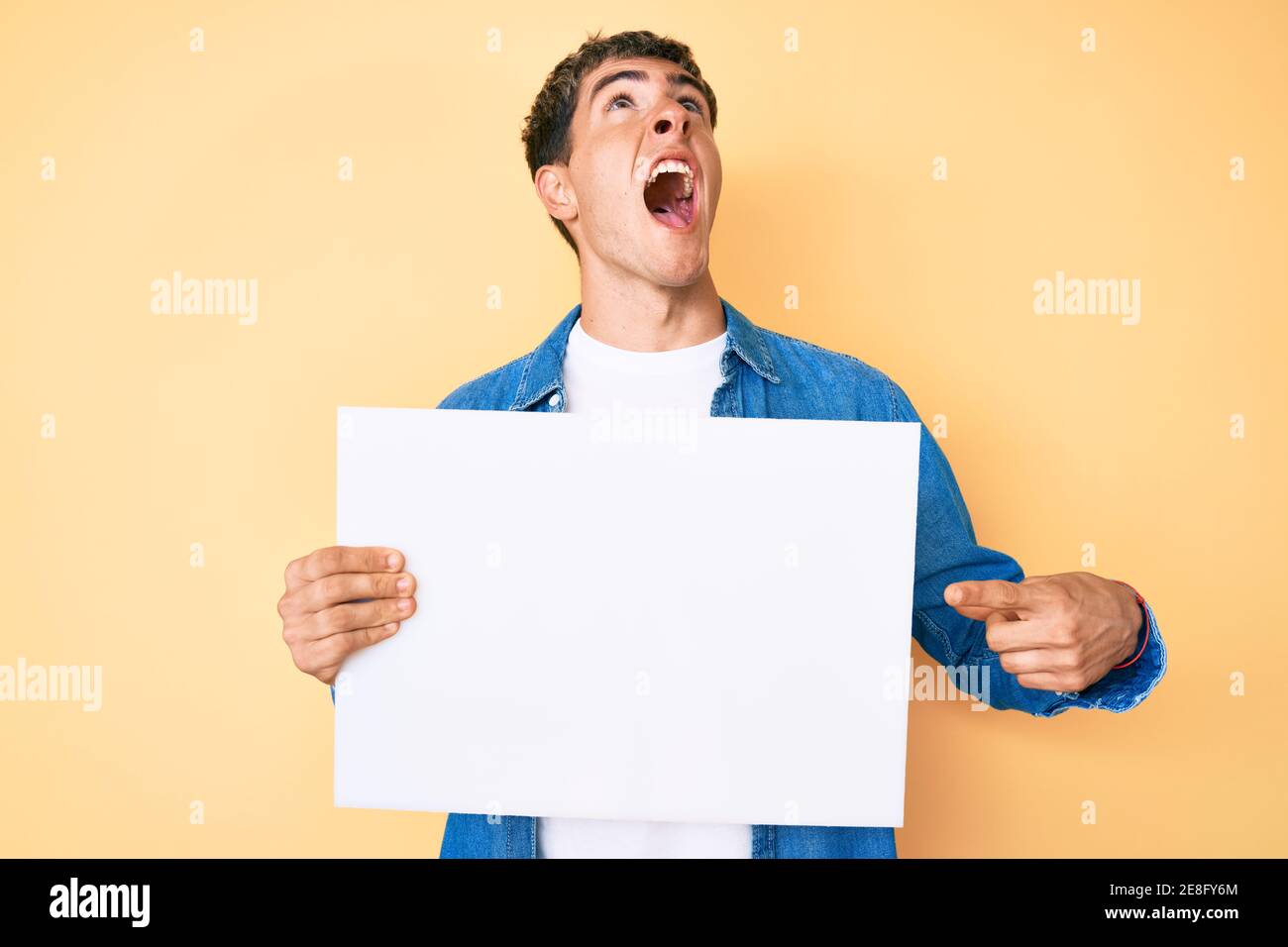 Young handsome man holding blank empty banner angry and mad screaming ...