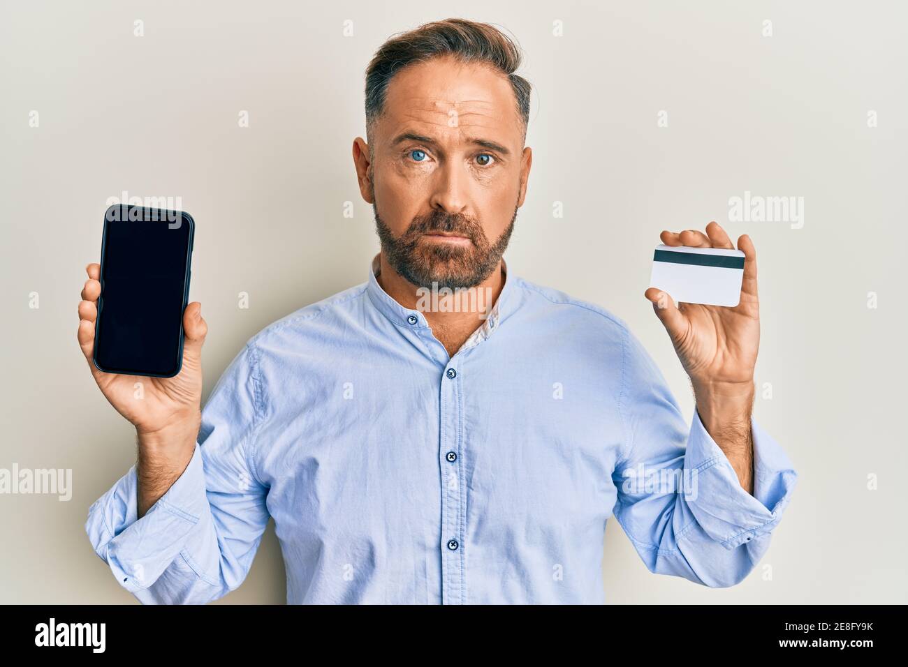 Handsome middle age man holding smartphone and credit card depressed ...