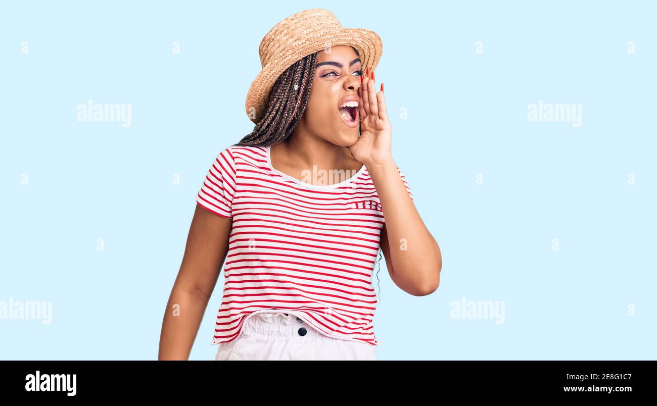 Young african american woman with braids wearing summer hat shouting ...