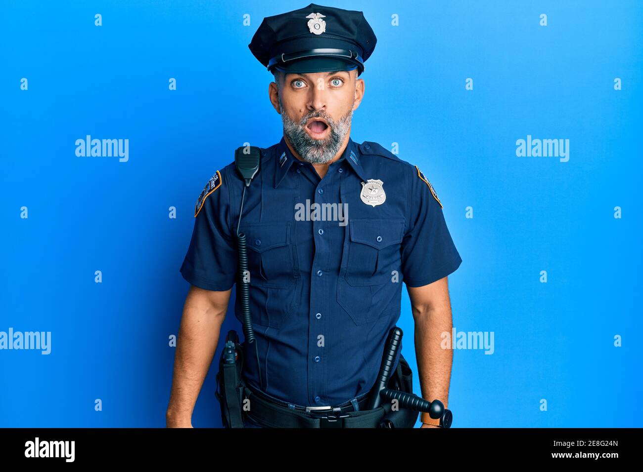 Middle age handsome man wearing police uniform afraid and shocked with ...