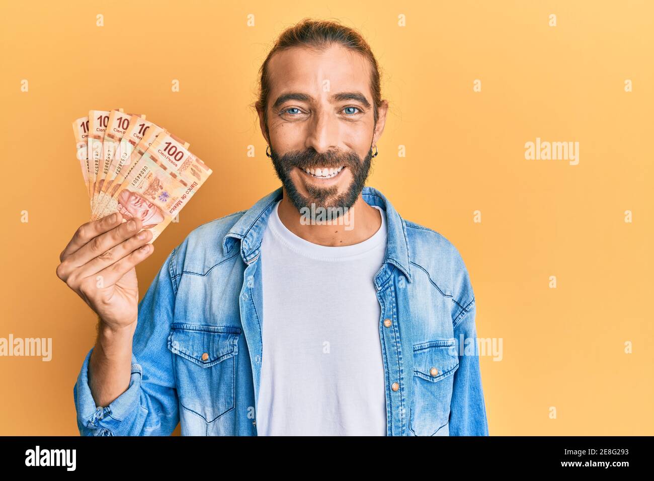 Attractive man with long hair and beard holding 100 mexican pesos ...