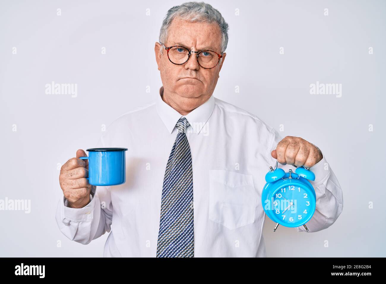Senior grey-haired man wearing business clothes holding alarm clock and ...