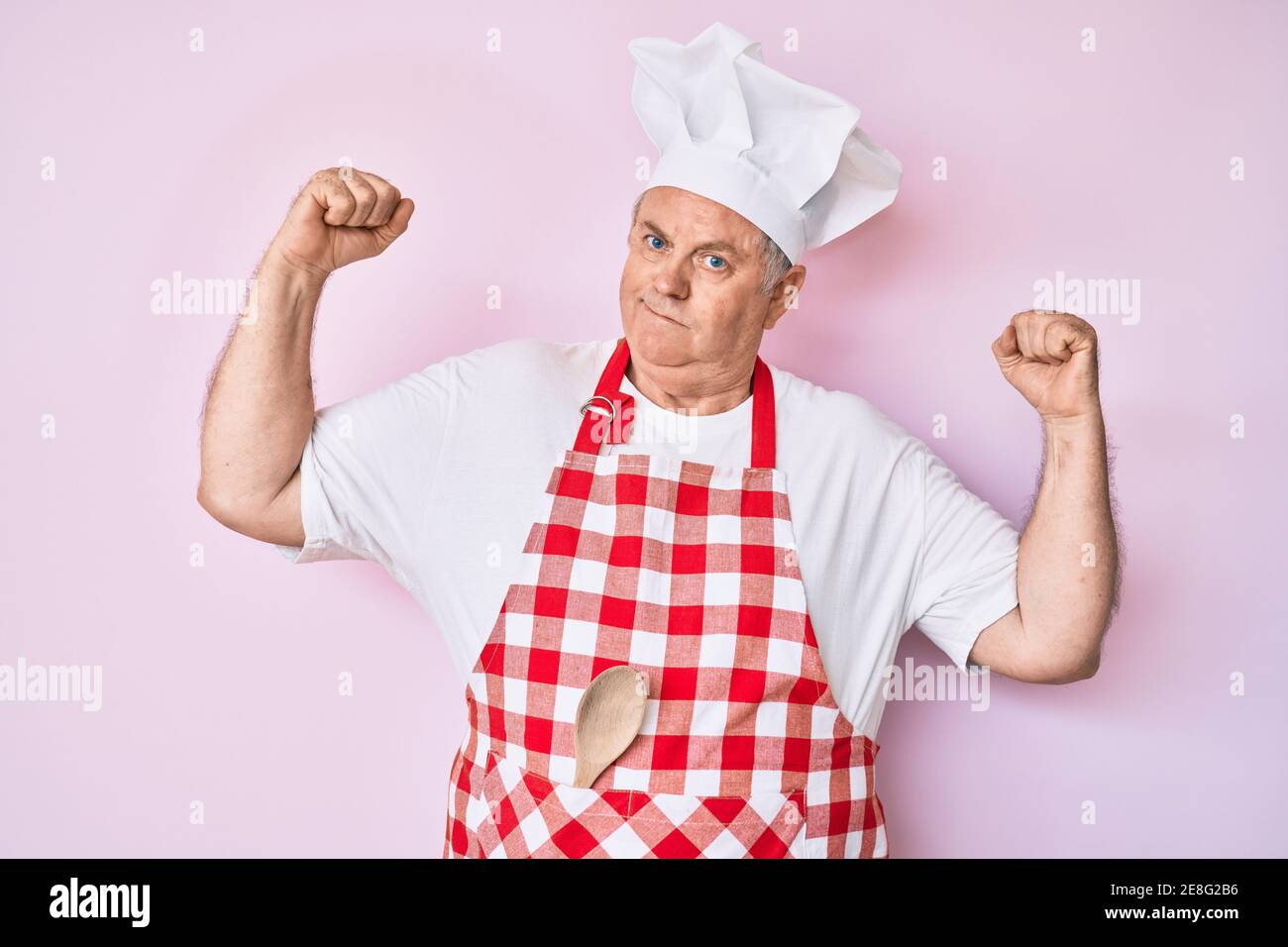 Senior grey-haired man wearing professional baker apron showing arms ...