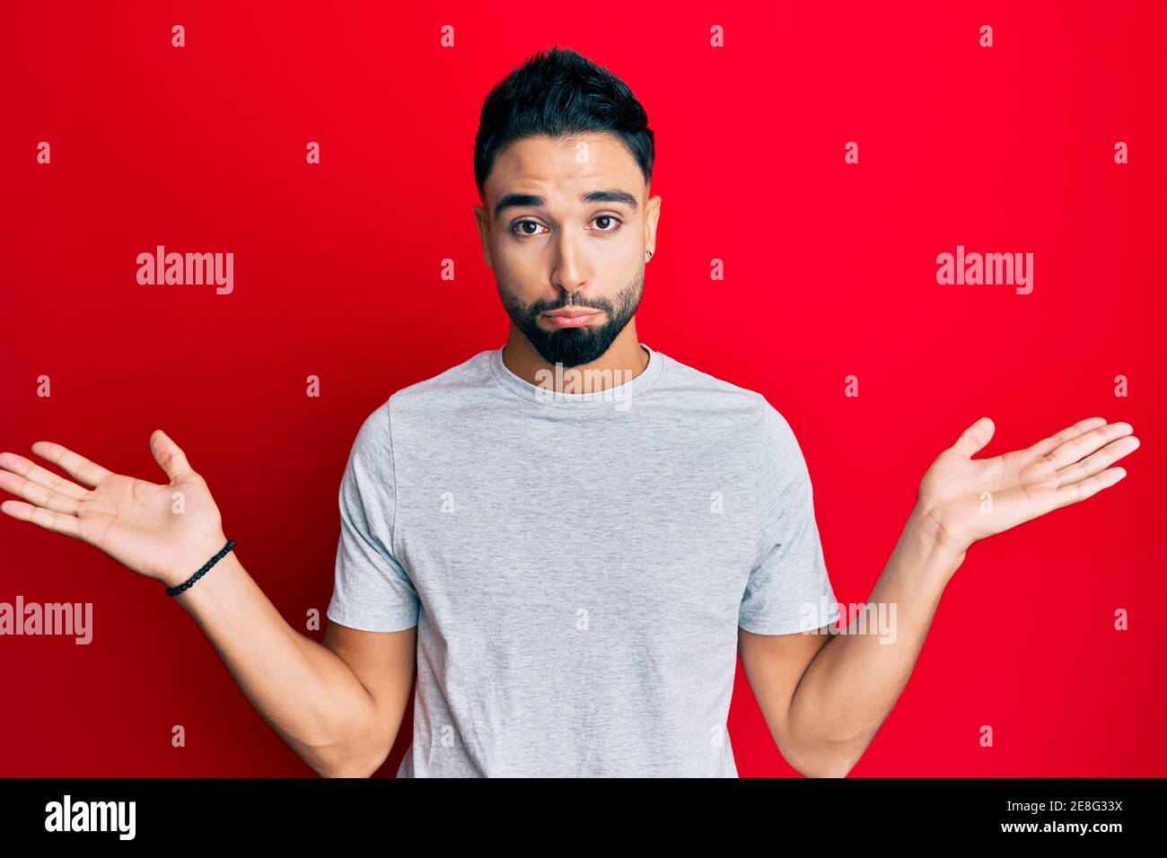 Young man with beard wearing casual white tshirt clueless and confused ...