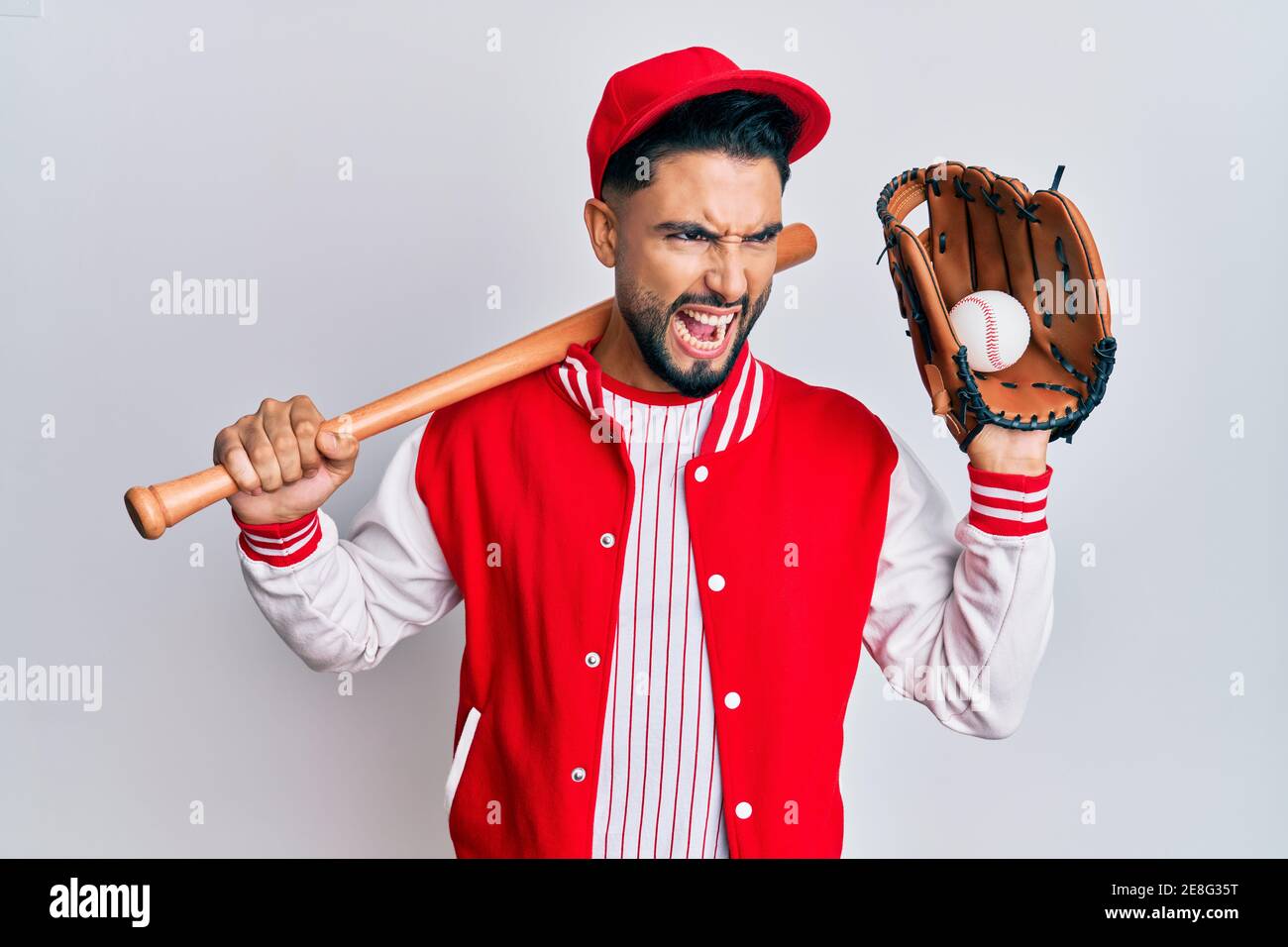 Young man with beard playing baseball holding bat and ball angry and ...