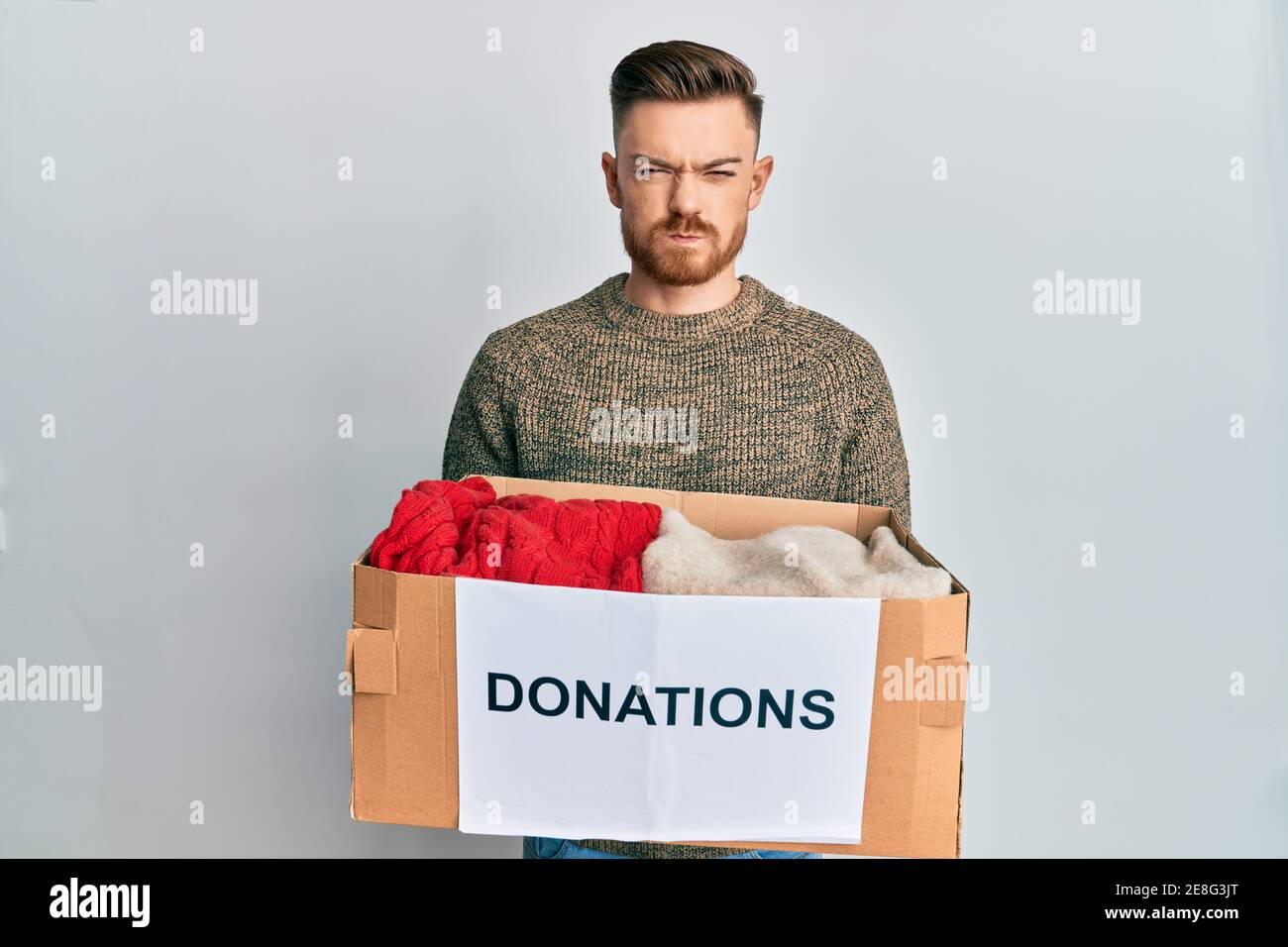 Young redhead man volunteer holding donations box puffing cheeks with ...