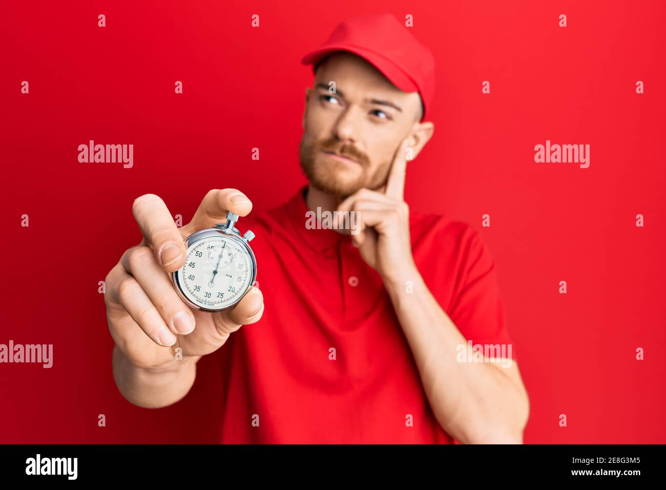 Young redhead man wearing delivery uniform and countdown clock serious ...
