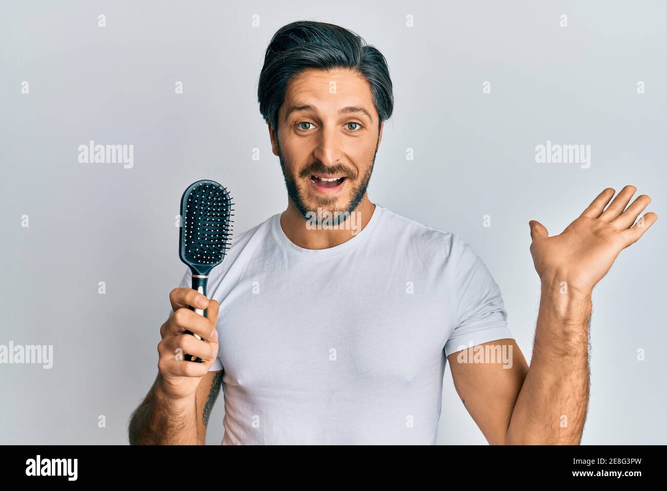 Young hispanic man styling hair using comb celebrating victory with ...