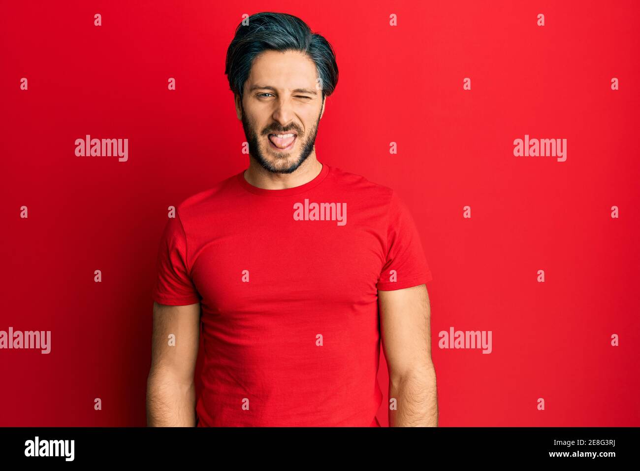 Young hispanic man wearing casual red t shirt sticking tongue out happy ...