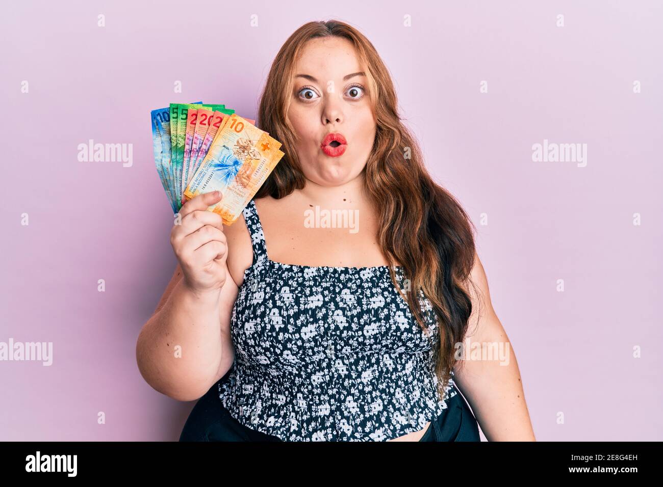 Plus size caucasian young woman holding swiss franc banknotes scared ...