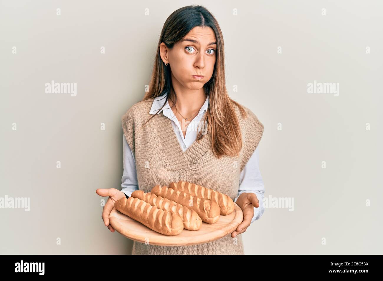 Brunette young woman holding homemade bread puffing cheeks with funny ...