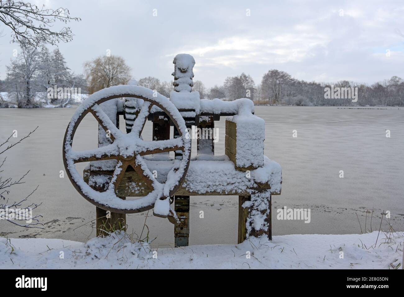 Snow-covered historic sluice wheel on a frozen dammed mill pond in ...