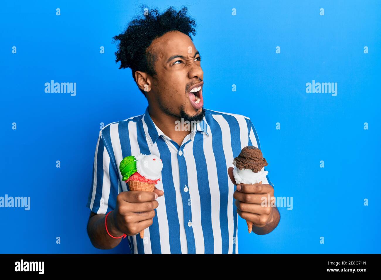 Young african american man with beard holding two ice cream cones angry ...