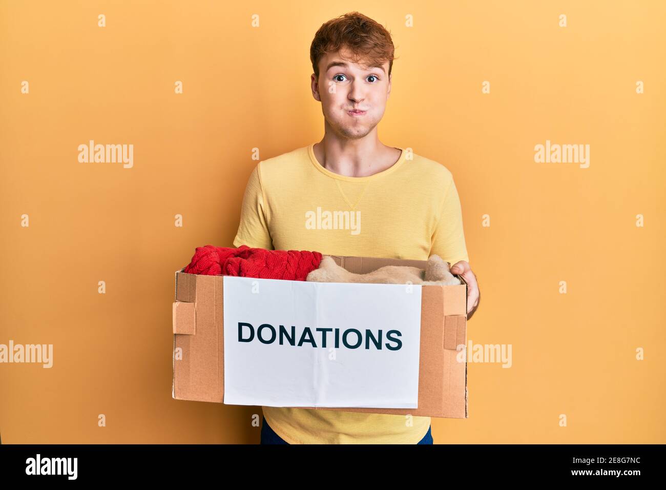 Young caucasian man holding donations box for charity puffing cheeks ...