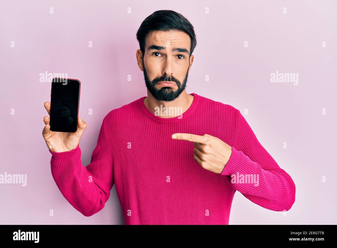 Young hispanic man holding smartphone showing blank screen depressed ...