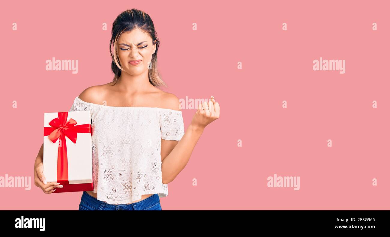 Young beautiful woman holding gift annoyed and frustrated shouting with ...