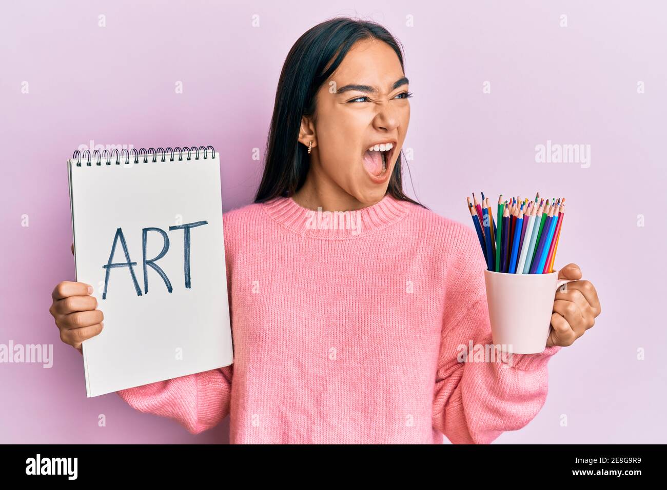 Young asian woman holding art notebook and colored pencils angry and ...