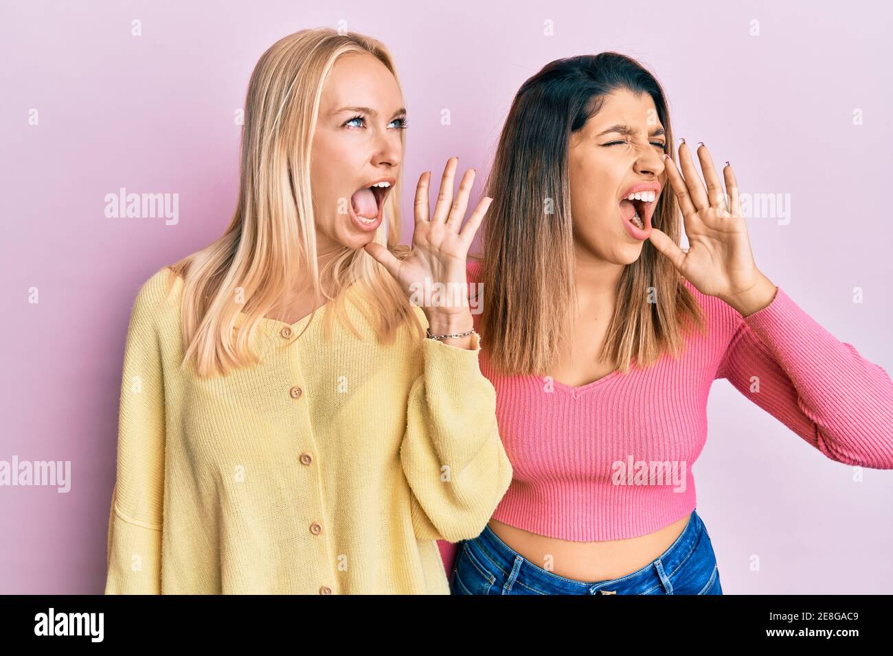 Two friends standing together over pink background shouting and ...