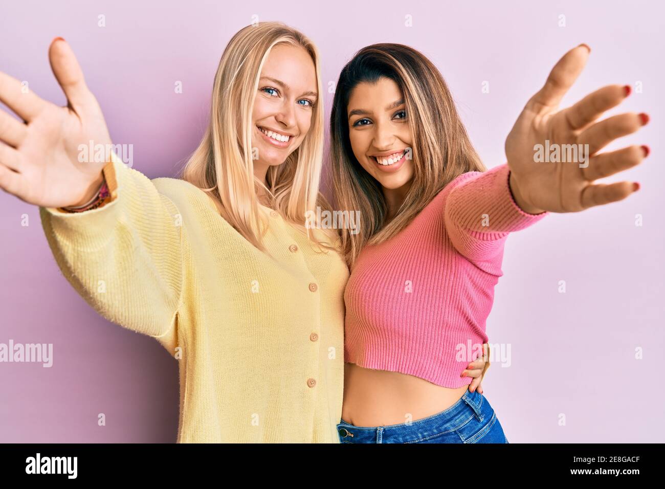 Two friends standing together over pink background looking at the ...