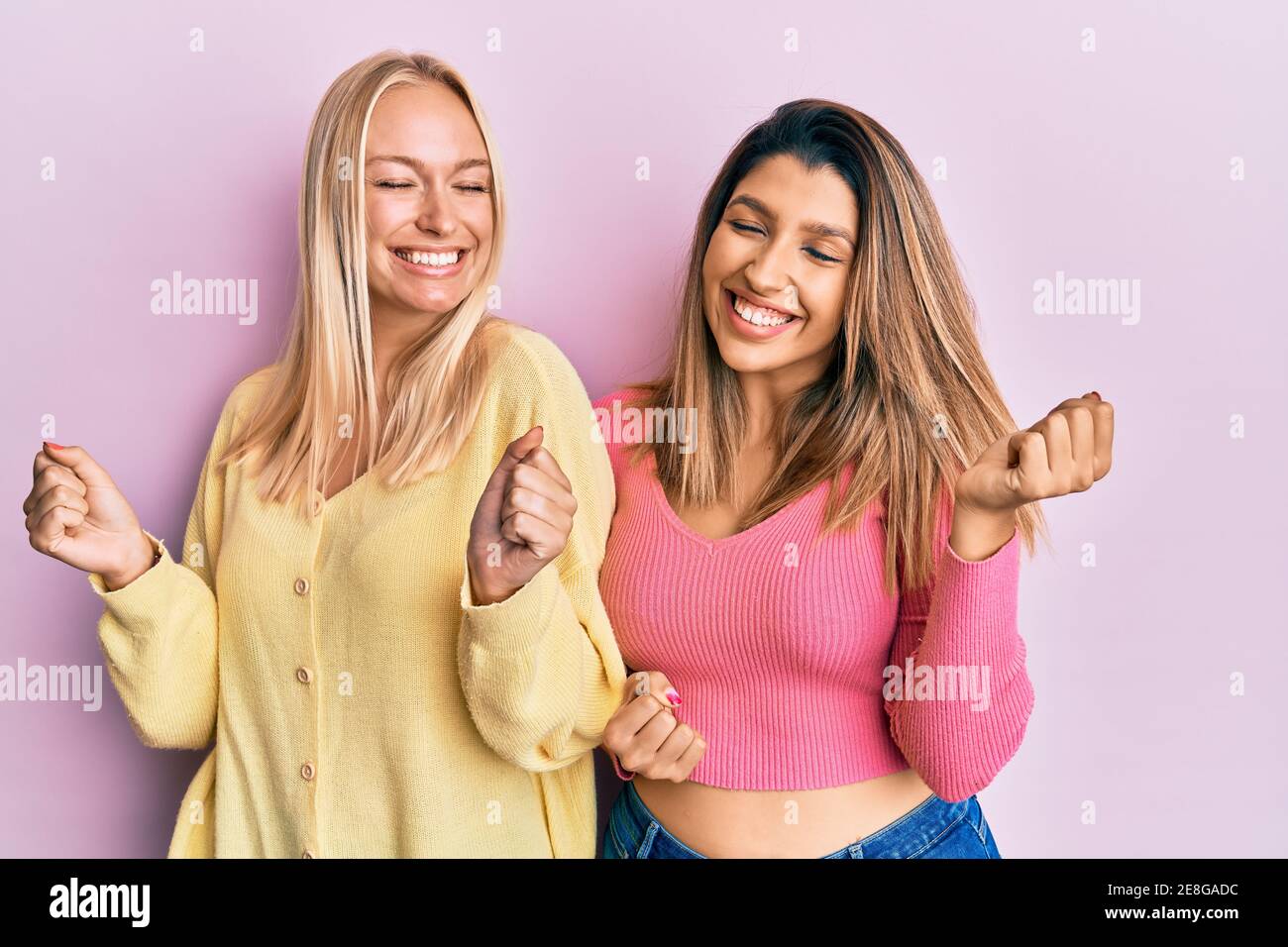 Two friends standing together over pink background excited for success ...