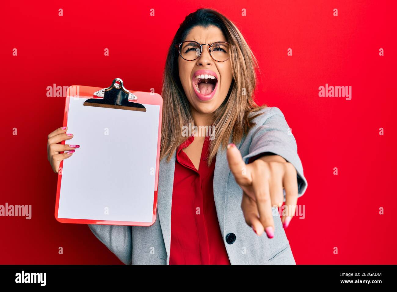Beautiful brunette woman holding clipboard with blank space angry and ...