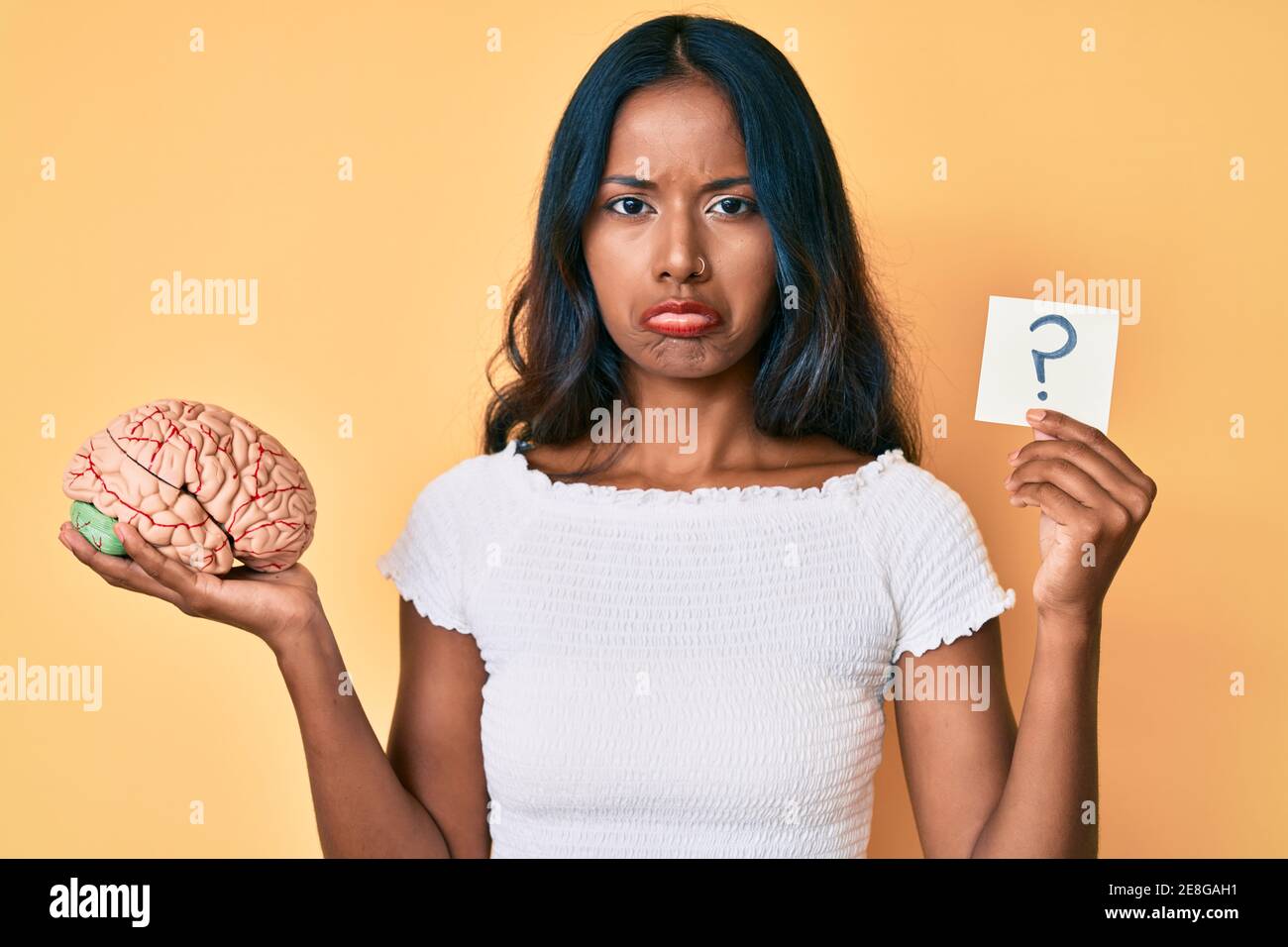 Young indian girl holding brain and question mark reminder depressed and worry for distress ...