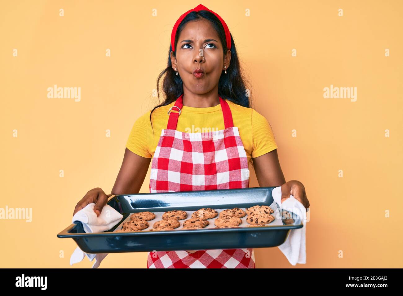 Young indian girl wearing baker uniform holding homemade cookies making ...