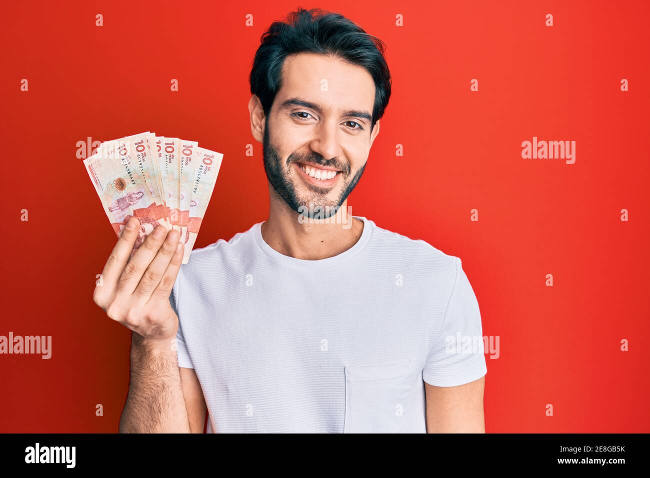 Young hispanic man holding 10 colombian pesos banknotes looking ...