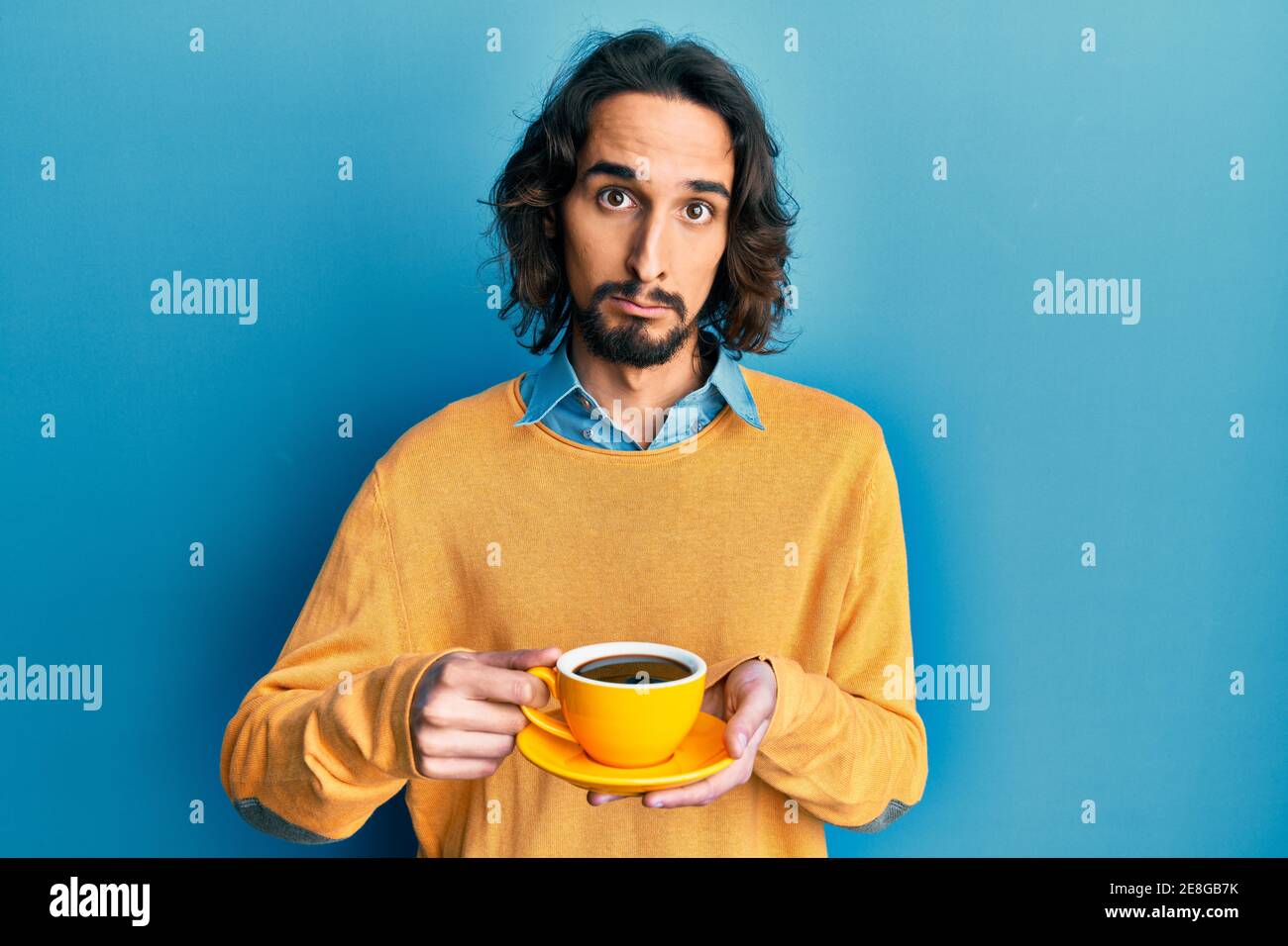 Young hispanic man drinking a cup of coffee depressed and worry for ...