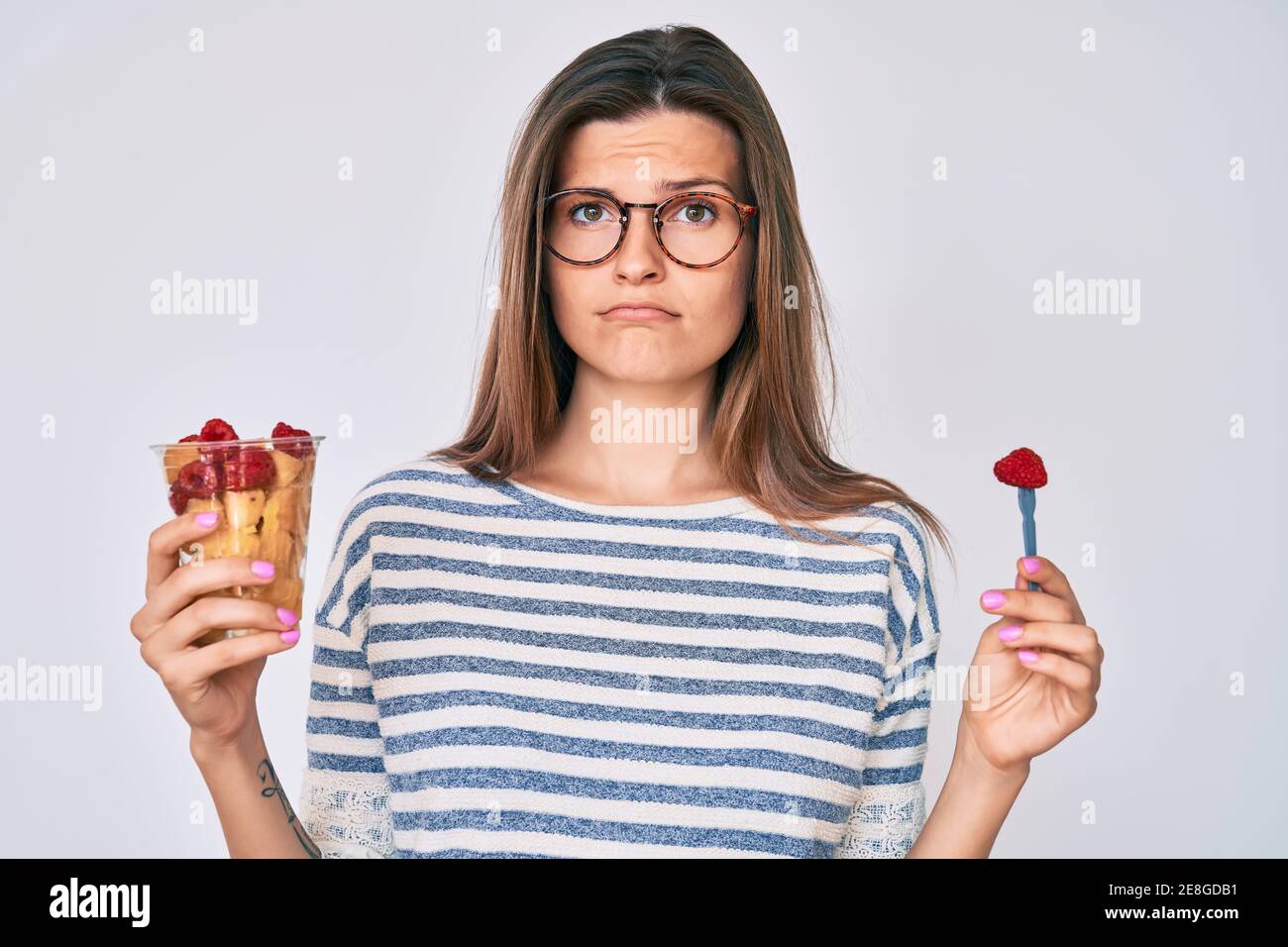 Beautiful caucasian woman eating fresh and healthy fruit skeptic and ...