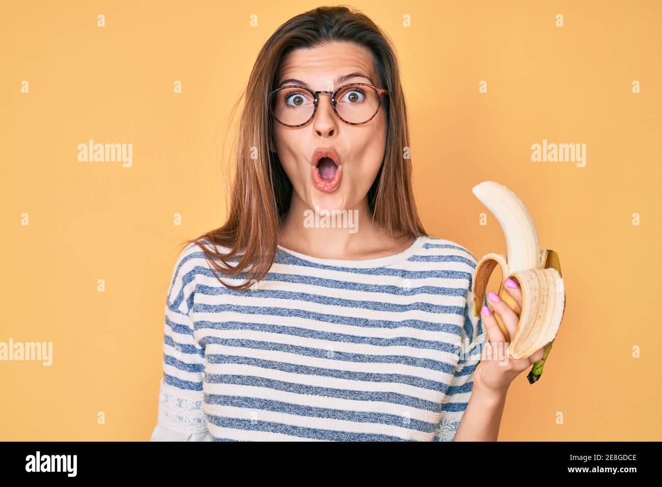 Beautiful caucasian woman eating banana as healthy snack scared and ...