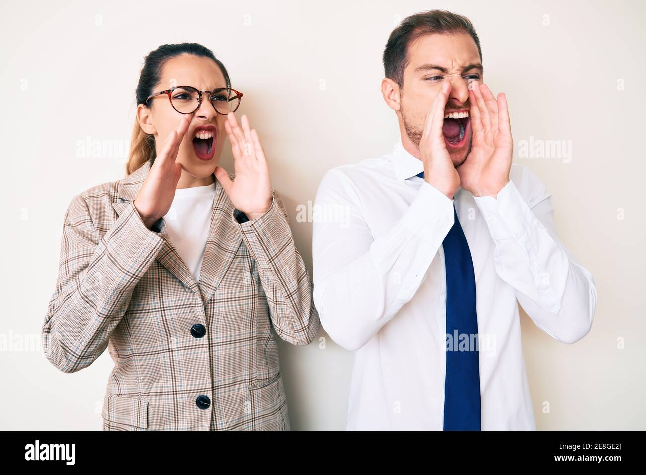 Beautiful couple wearing business clothes shouting angry out loud with ...