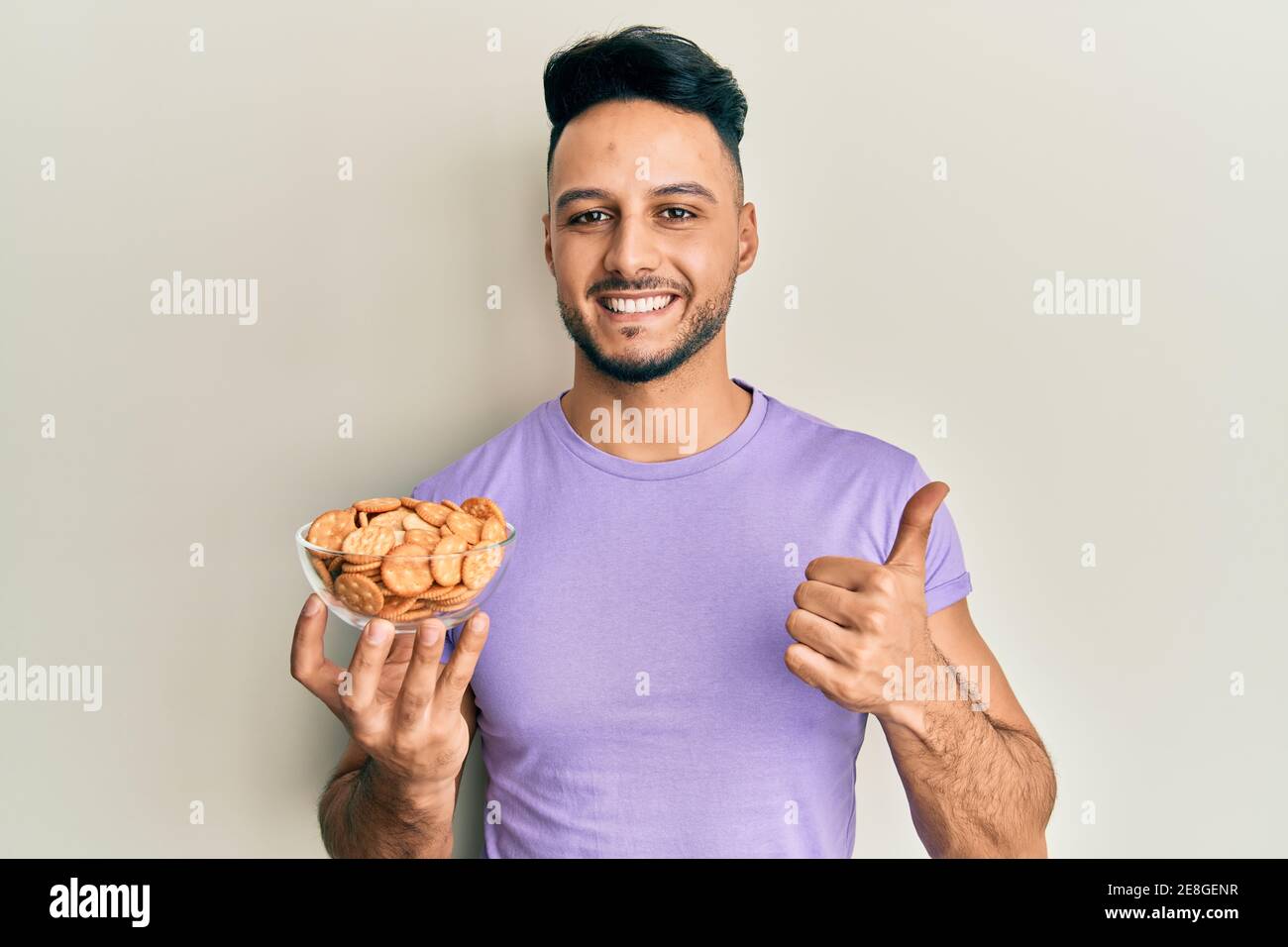 Young arab man holding bowl of salty crackers biscuits smiling happy ...