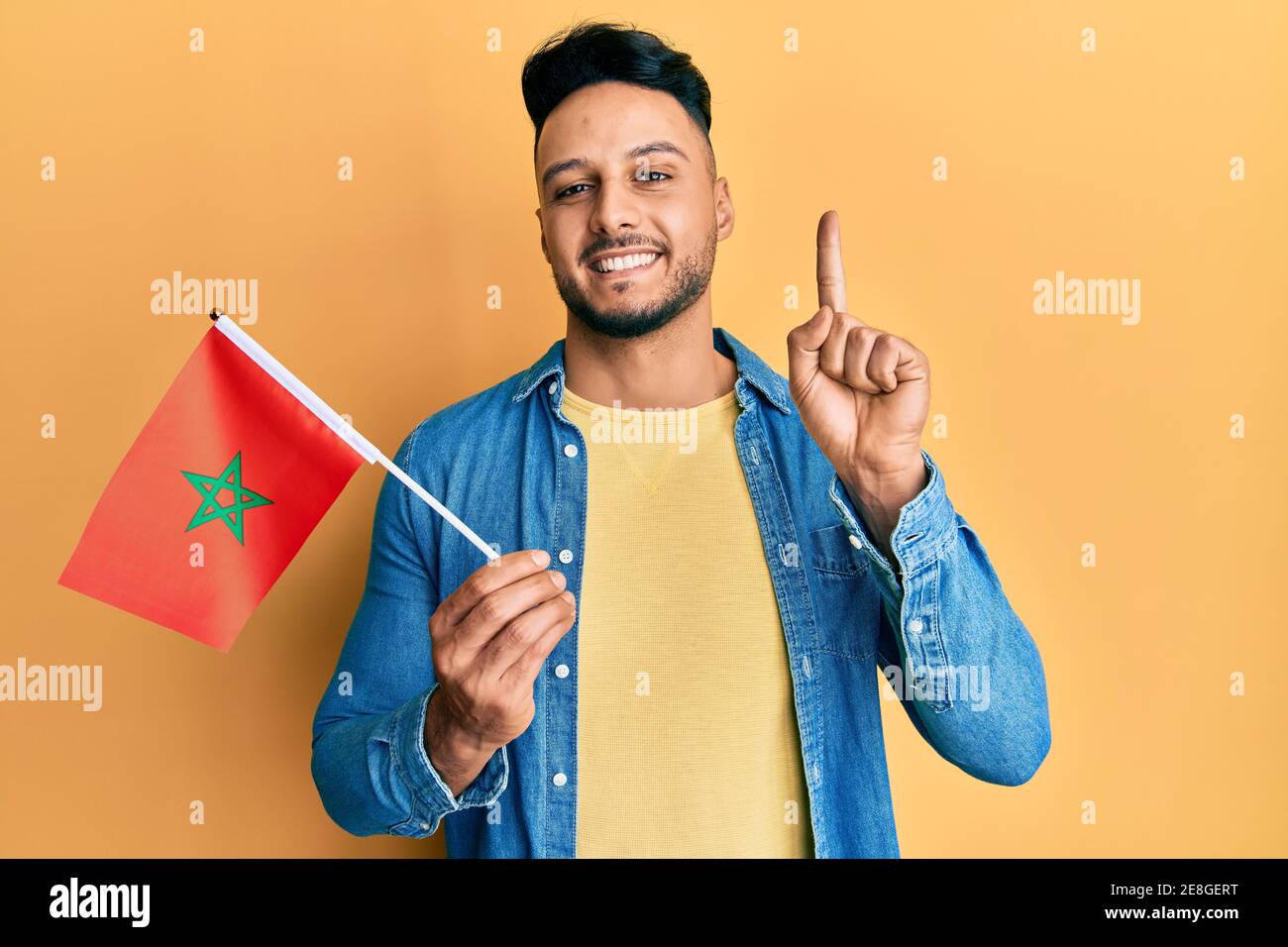 Young arab man holding morocco flag smiling with an idea or question ...