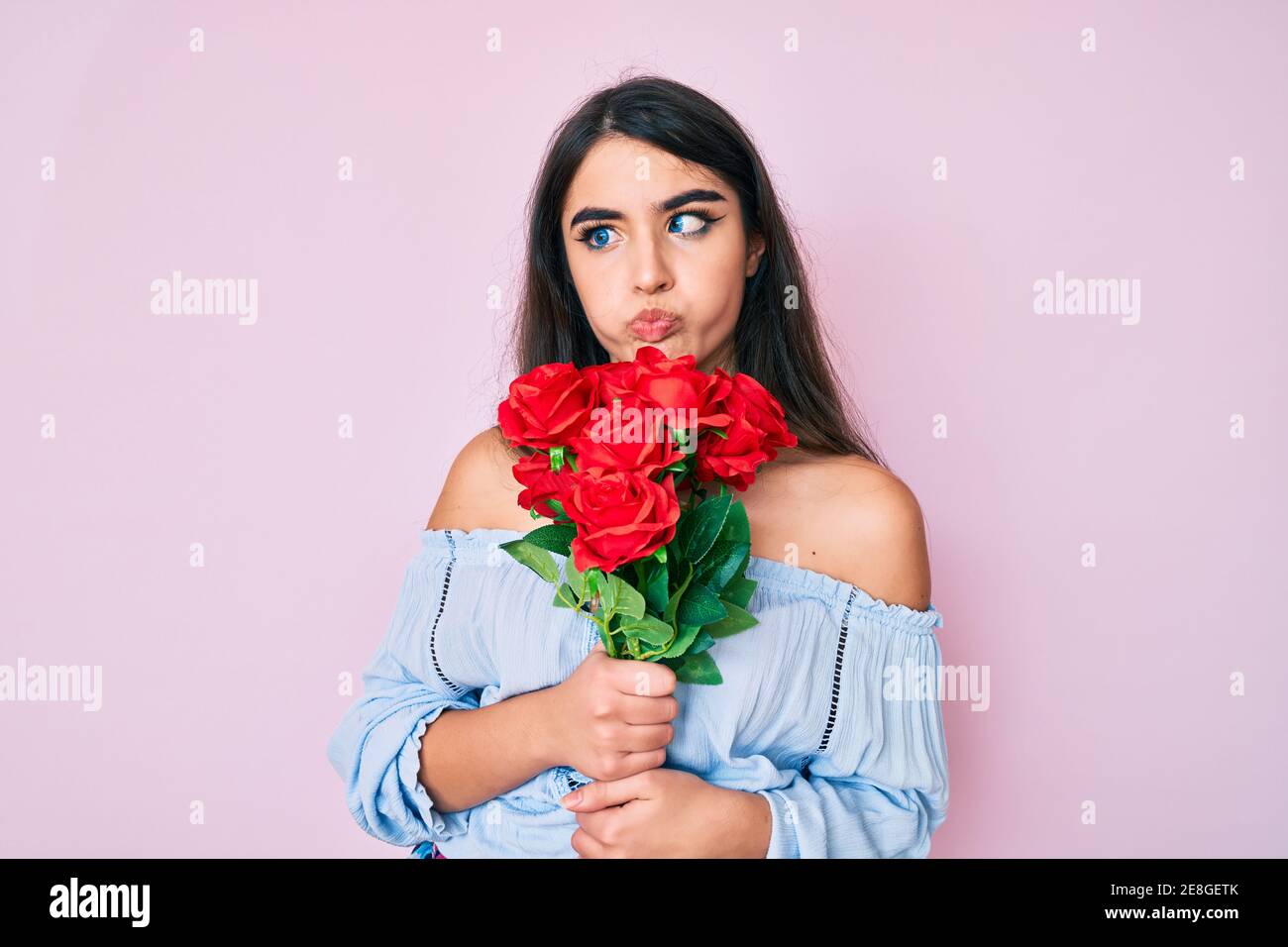 Brunette teenager girl holding flowers making fish face with mouth and ...