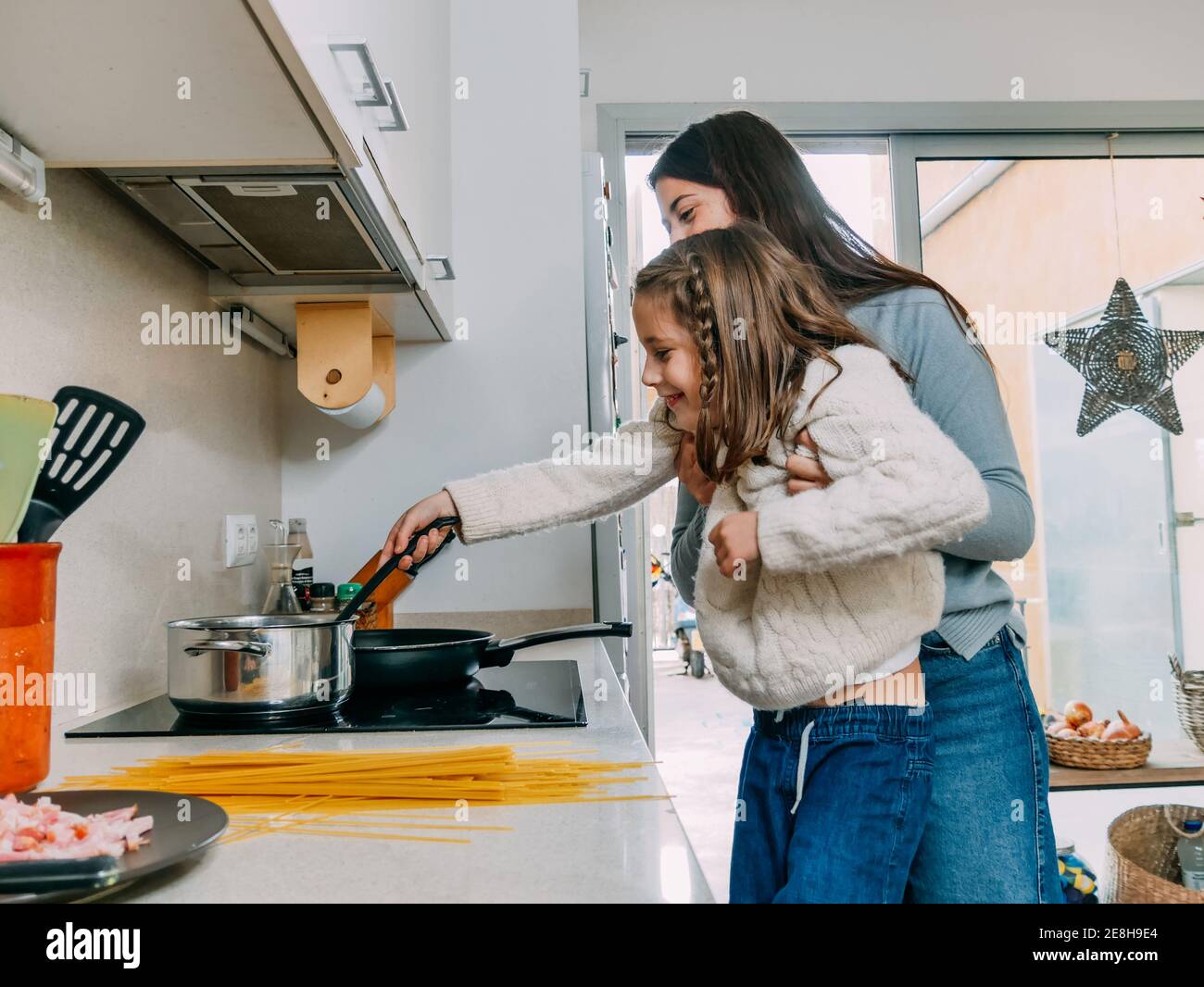 Cheerful young mother lifting cute smiling daughter stirring food on ...