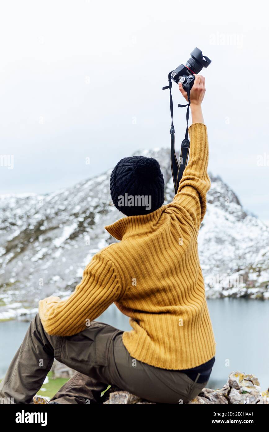 Back view full body photographer in warm clothes raising arm with photo ...