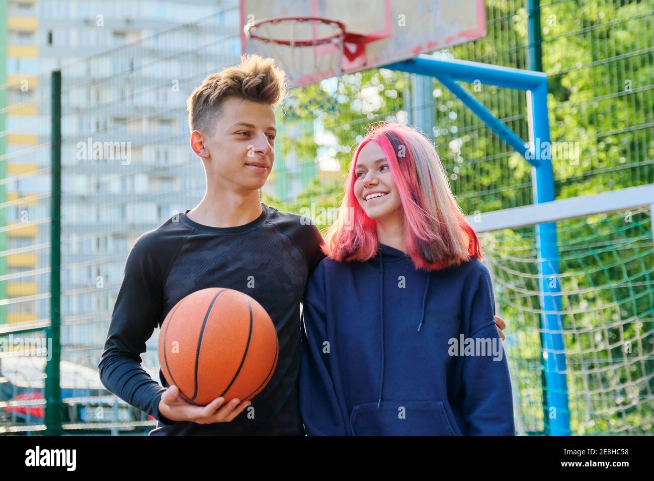 Portrait of guy and teenage girl hugging on basketball court with ball ...