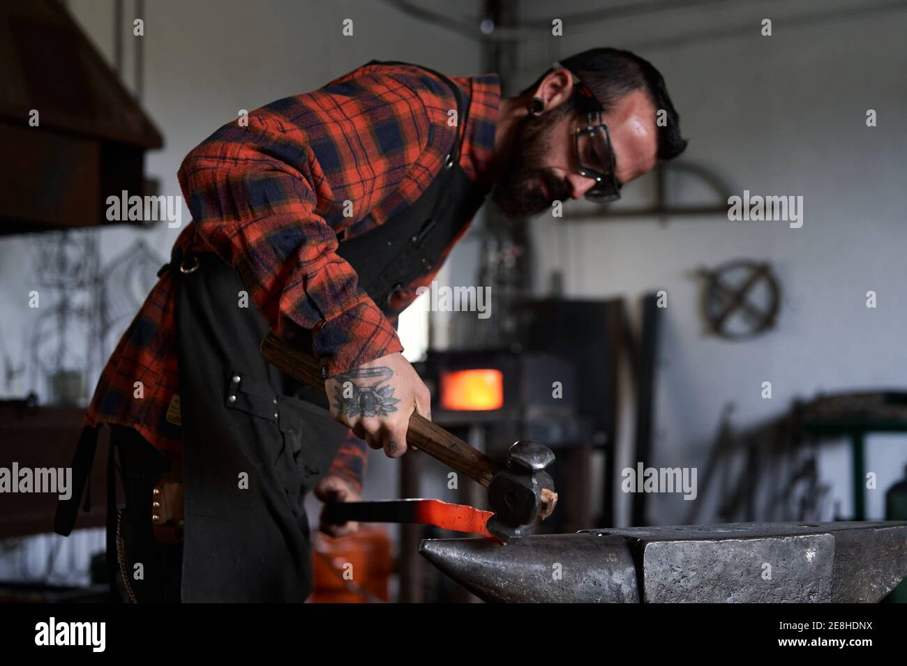Side view of young brutal bearded craftsman in apron and goggles ...