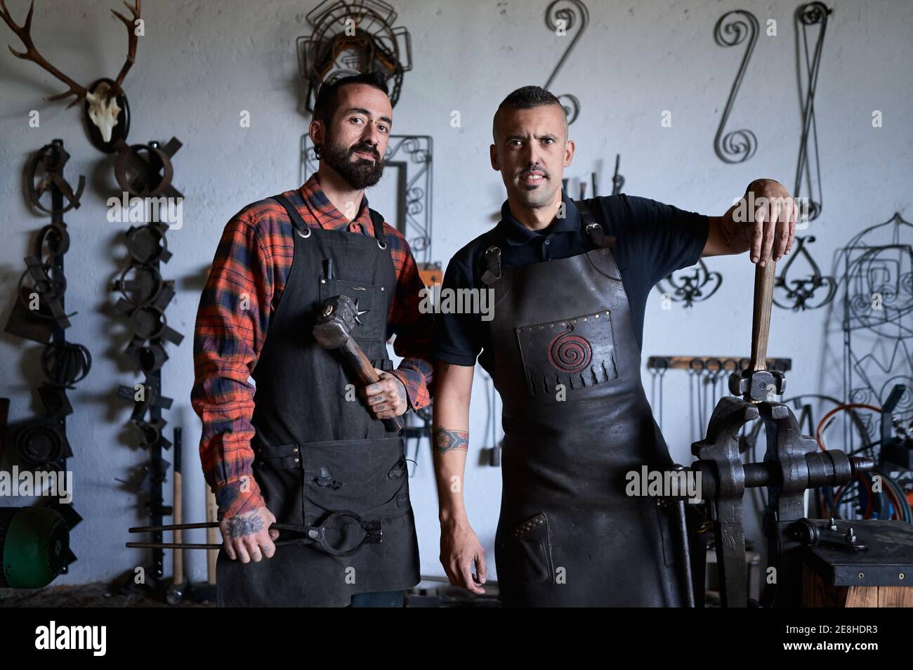 Young brutal ethnic male blacksmiths in casual clothes and aprons ...
