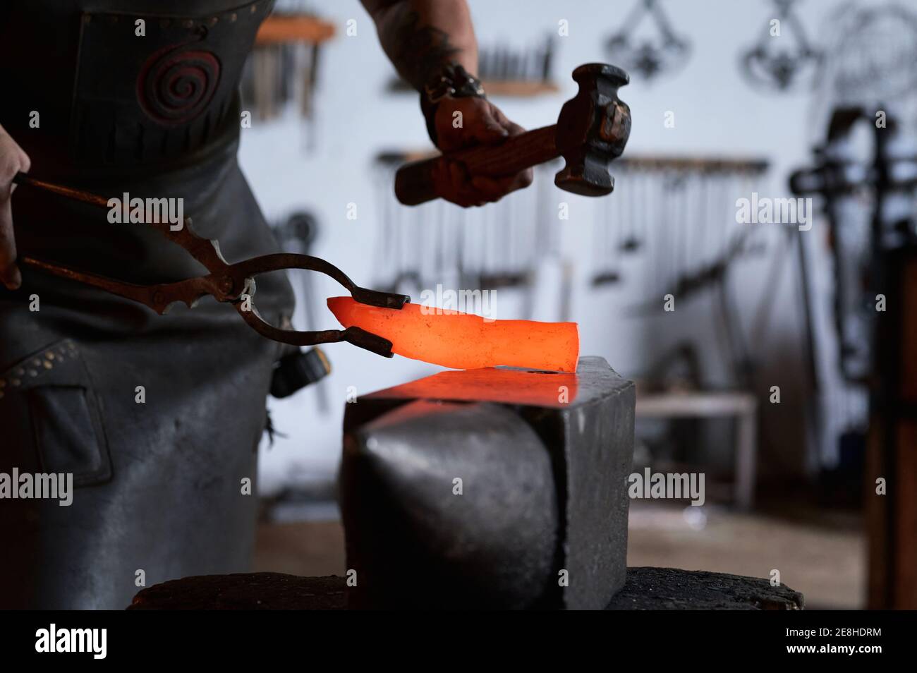 Side view of anonymous tattooed young male forger in apron heating ...