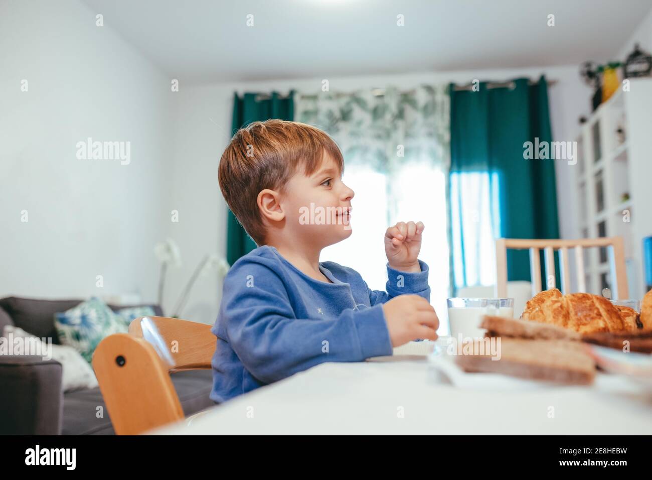 Side view of small smiling child sitting on chair at table with milk ...