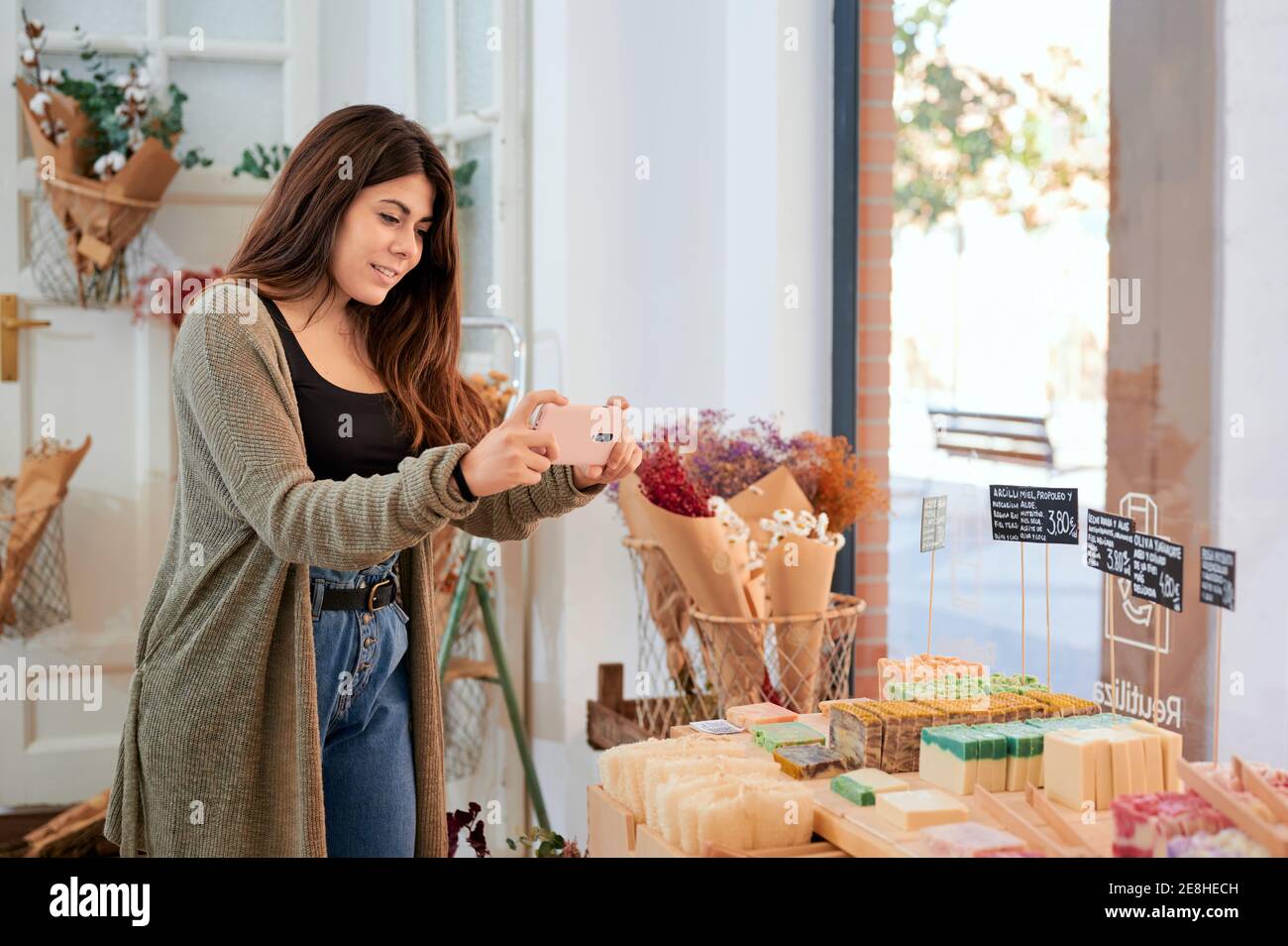 Smiling female taking photo of organic soap selling in bulk store with ...