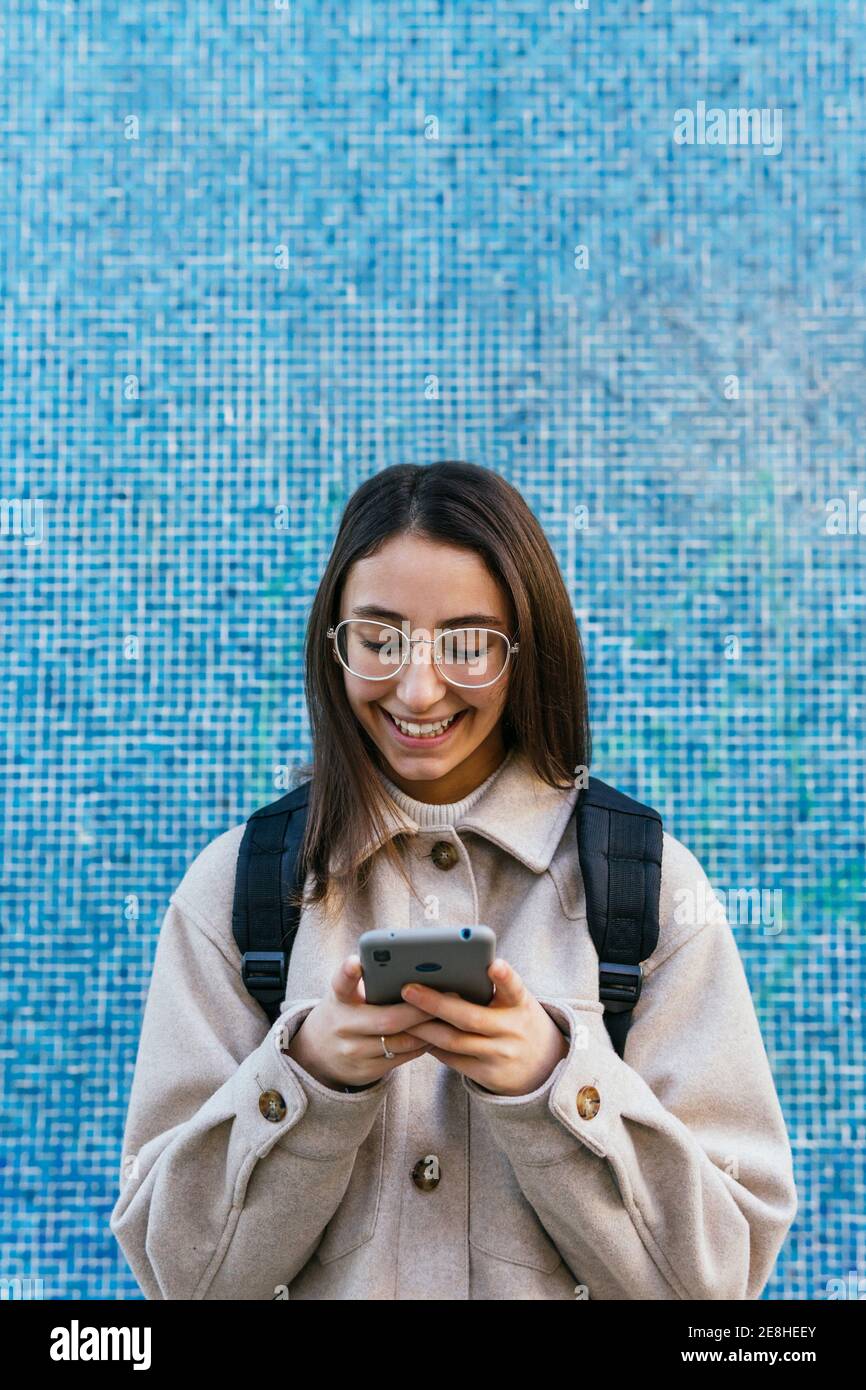 Crop attractive smiling female student in warm wear with backpack using ...